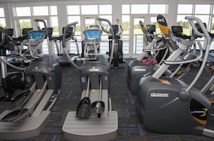 Uma academia com vários equipamentos de cardio, incluindo esteiras e elípticos, dispostos em fileiras.
