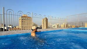Uma piscina com uma pessoa na água, cercada por edifícios altos e um céu claro.