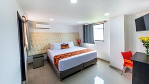 Quarto de hotel moderno com uma cama grande, uma escrivaninha, uma cadeira e uma televisão.