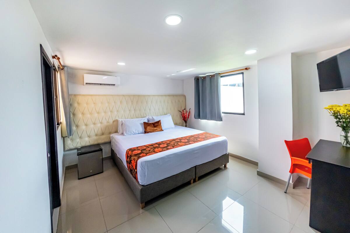 Quarto de hotel moderno com uma cama grande, uma escrivaninha, uma cadeira e uma televisão.