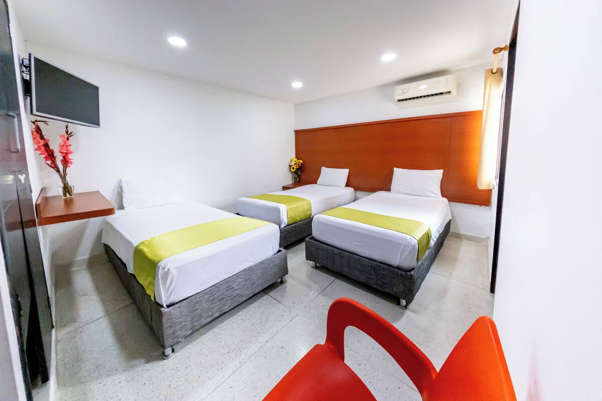 Quarto de hotel com duas camas, uma escrivaninha, uma televisão e ar condicionado.