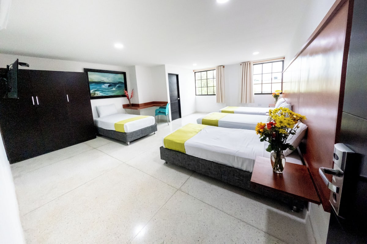 Quarto de hotel com duas camas, uma escrivaninha, uma TV e uma janela grande.