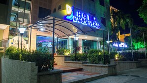Entrada de hotel com varanda coberta, placa indicando ser um hotel de DJ e fachada bem iluminada.