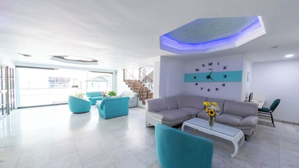 Uma sala de estar moderna com um relógio grande, sofás verde-água e cinza, e uma mesa de centro.
