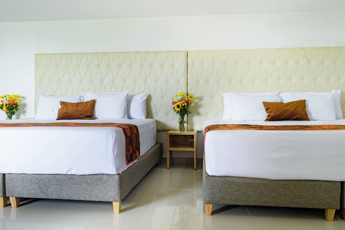 Quarto de hotel com duas camas, uma mesa de cabeceira e um vaso de flores.