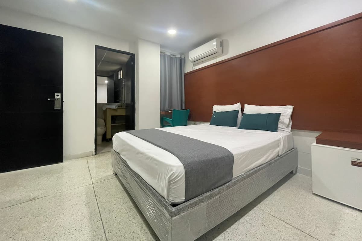 Quarto de hotel moderno com uma cama grande, cabeceira de madeira, uma escrivaninha pequena e um guarda-roupa branco.