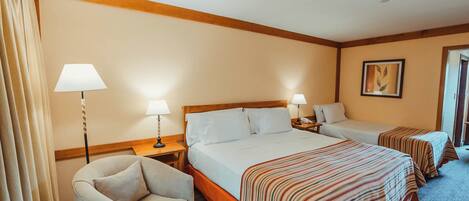 Quarto de hotel com uma cama grande, duas mesas de cabeceira, uma cadeira e uma escrivaninha.