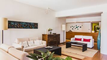 Uma sala de estar moderna com um sofá bege, uma mesa de centro preta e um quadro grande de peixes na parede.