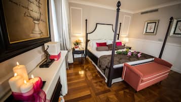 Uma cama de dossel com cabeceira, uma mesa de cabeceira com abajur, uma pequena mesa com um vaso de flores e um banco vermelho.