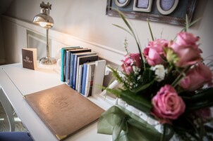 Uma mesa com abajur, livros, um cartão e um buquê de flores.