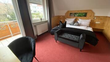 Um quarto com uma cama, uma poltrona preta, cabeceira de madeira, uma janela com persianas e um tapete vermelho.