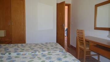 Quarto com cama, guarda-roupa de madeira e escrivaninha com cadeira.