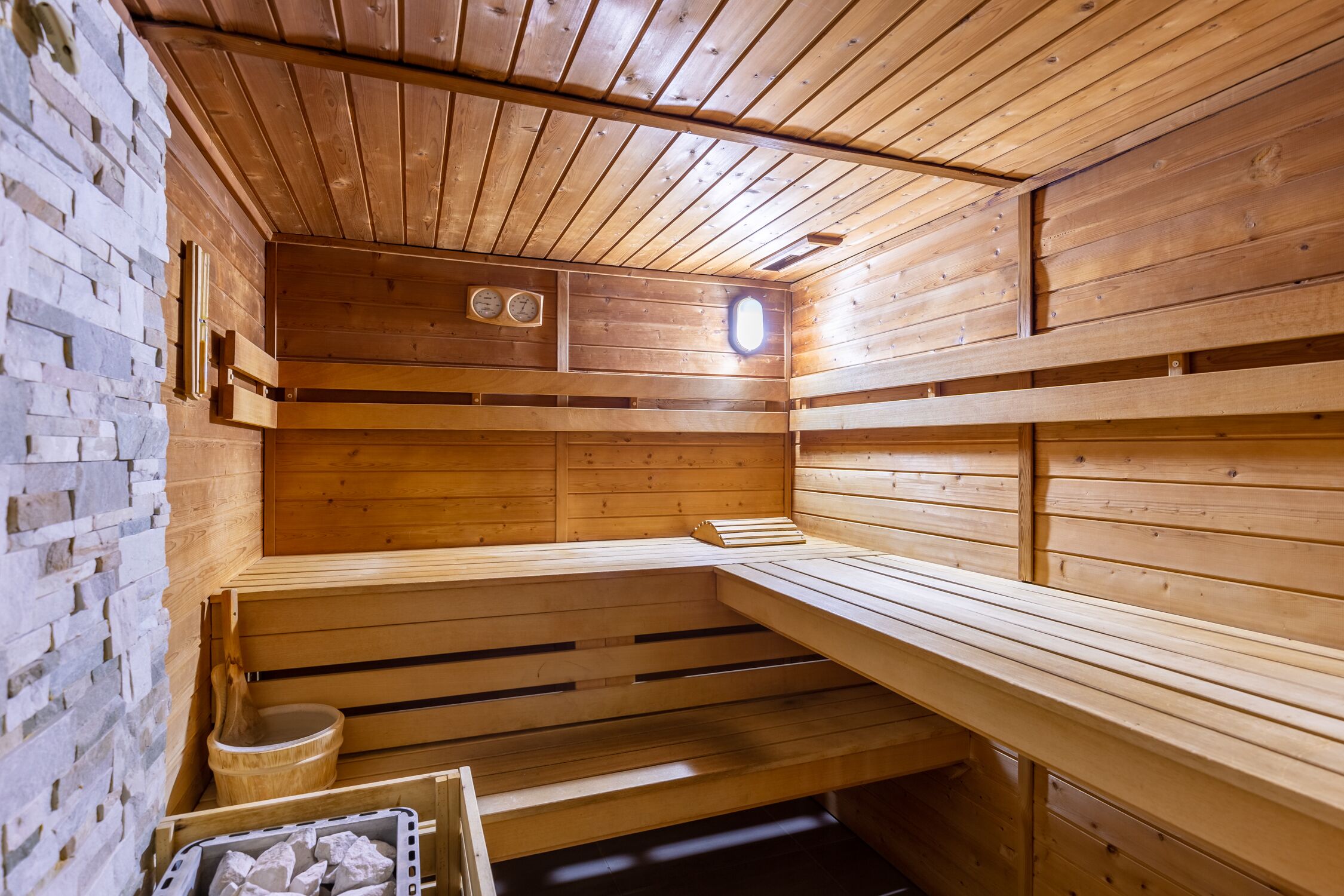 Uma sauna com bancos de madeira, parede de pedra e teto de madeira.