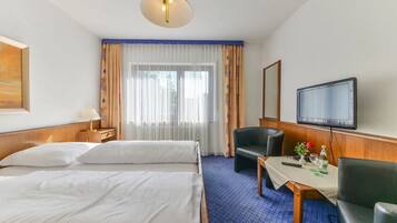 Quarto de hotel com duas camas, uma secretária com cadeira, televisão e janela com cortinas.