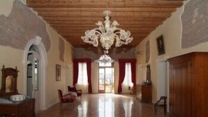 Um quarto amplo com teto de madeira, um candelabro e uma grande janela com cortinas vermelhas.