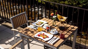 Uma mesa de madeira com uma cadeira branca, posta com pratos de comida, um copo de suco, uma xícara de café e um vaso com flores.