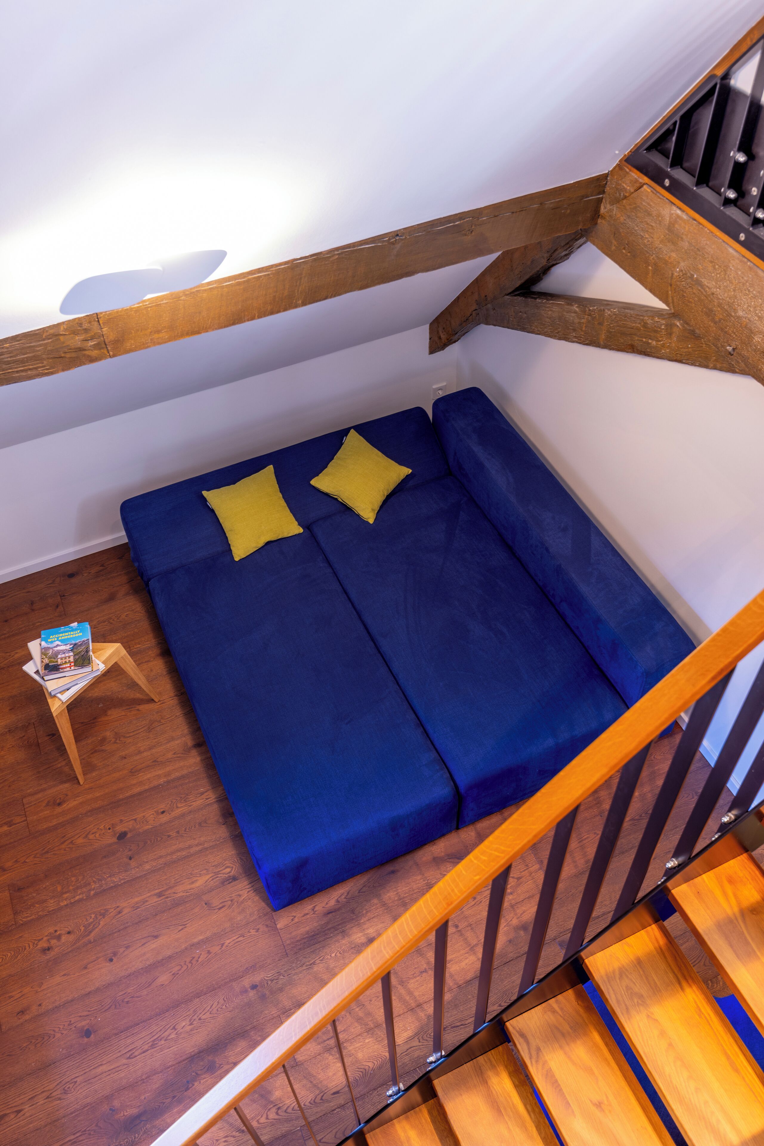 Quarto com sofá azul, piso de madeira e pequena mesa de madeira com um livro.