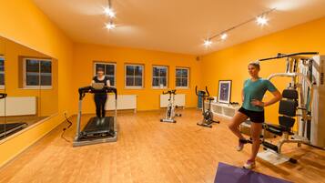 Uma academia com equipamentos de exercício, esteira e um espelho.