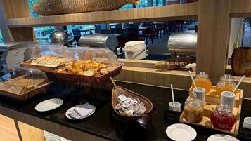 Uma área de buffet com diversos alimentos, incluindo pães, doces e bebidas.