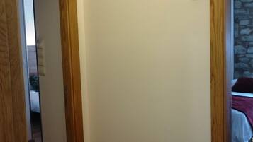 Um corredor com piso de madeira e uma porta que dá para um quarto com parede de pedra. Uma placa com o número 301 é visível na parede.