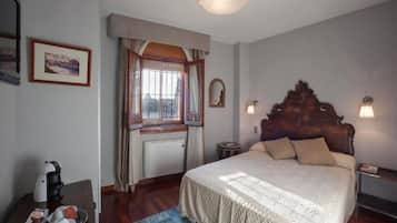 Quarto de hotel com uma cama grande, cabeceira de madeira, mesa de cabeceira, janela com cortinas, radiador, espelho fixado na parede e luminária no teto.