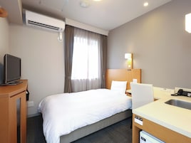 Quarto de hotel com cama, escrivaninha com cadeira, televisão, pia e ar condicionado.
