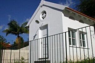 Um edifício branco com uma janela circular e uma porta, cercado por uma cerca de metal preta.