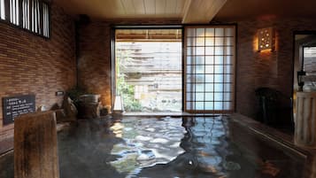 Um onsen japonês tradicional com interior de madeira, uma bacia de pedra e vista para o exterior através de uma porta deslizante.
