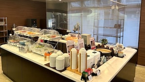 Uma área de buffet com estações de comida cobertas, um espaço para café e diversas opções de temperos e utensílios.