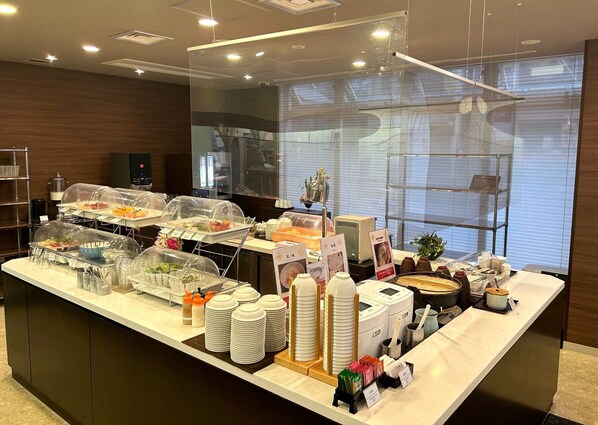 Uma área de buffet com estações de comida cobertas, um espaço para café e diversas opções de temperos e utensílios.