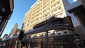 Um hotel de vários andares com design moderno, apresentando varandas em cada pavimento e uma entrada imponente com galeria coberta.