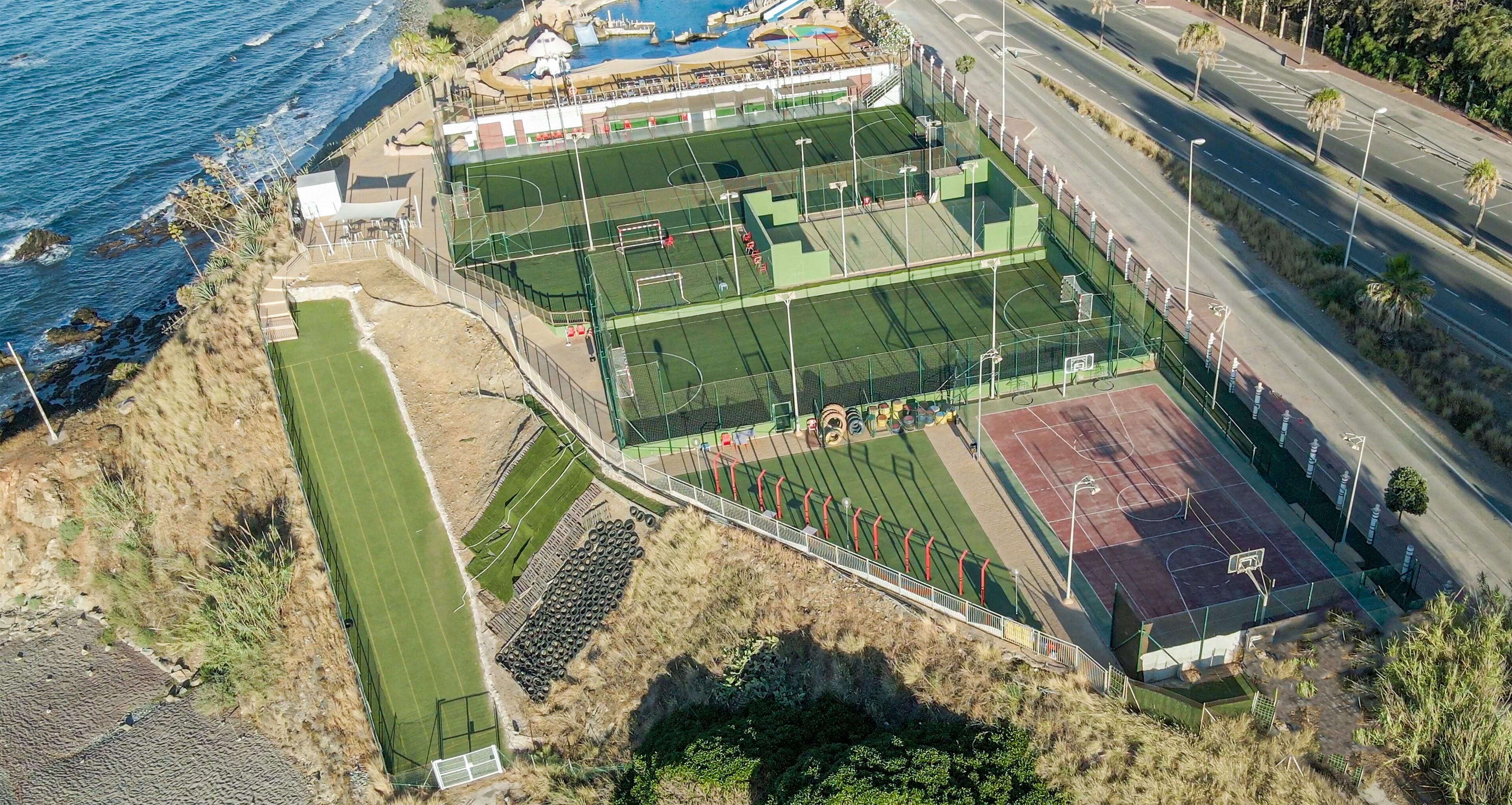 Vista aérea de um complexo esportivo com várias quadras de tênis, uma piscina e uma estrada ao lado do local.
