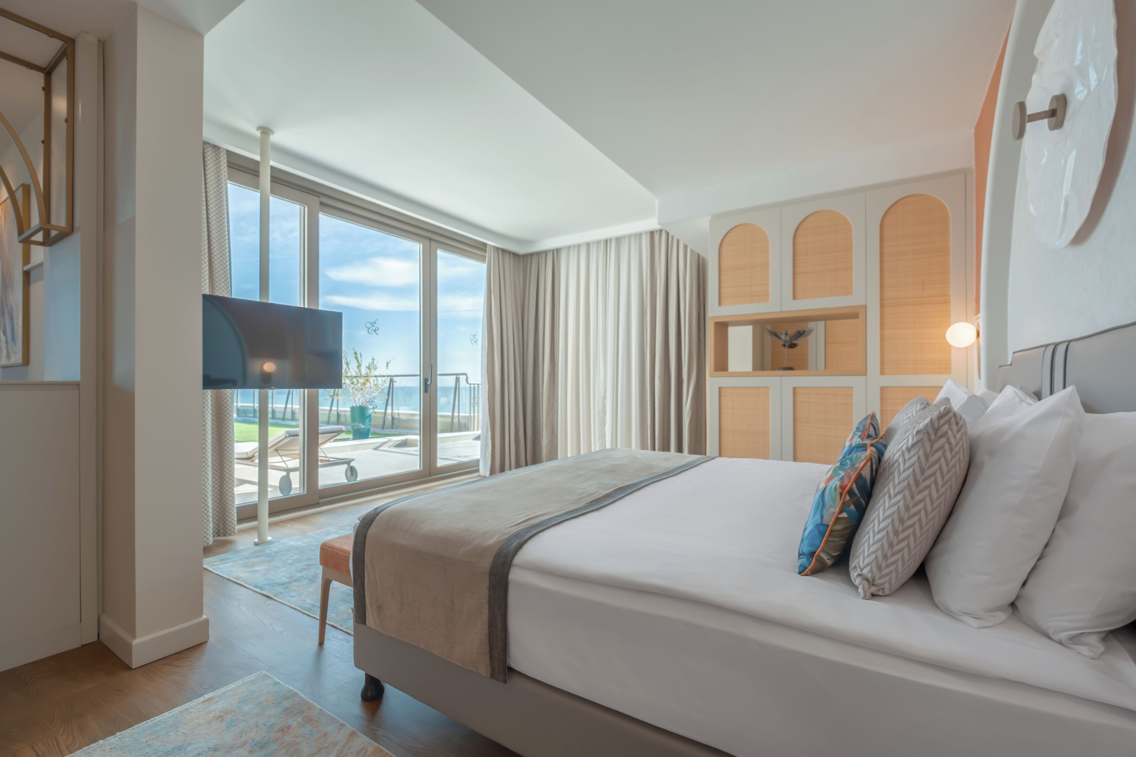 Quarto de hotel com uma cama grande, televisão, varanda com vista e painel de parede de madeira.