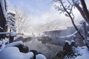 Uma onsen japonesa tradicional, com uma nascente termal rodeada por rochas e árvores cobertas de neve.