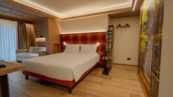 Quarto de hotel com uma cama grande, uma escrivaninha, uma cadeira, mesa de cabeceira e um quadro na parede.