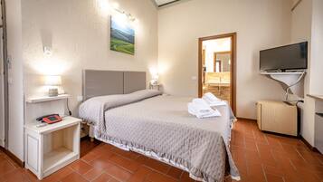 Quarto com cama, abajures, televisão de tela plana, um pequeno armário e um quadro na parede.