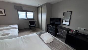 Quarto de hotel com duas camas, uma cadeira, cômoda, televisão e janela com persianas.