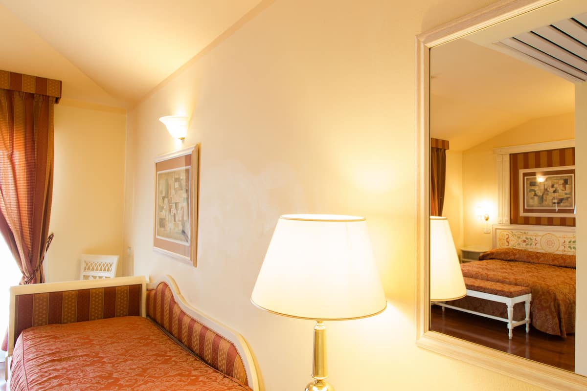 Quarto de hotel com cama, luminária de cabeceira, cadeira e um espelho grande que reflete o aposento.