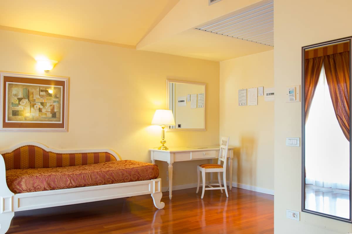Quarto com cama, escrivaninha, cadeira e janela com cortinas.