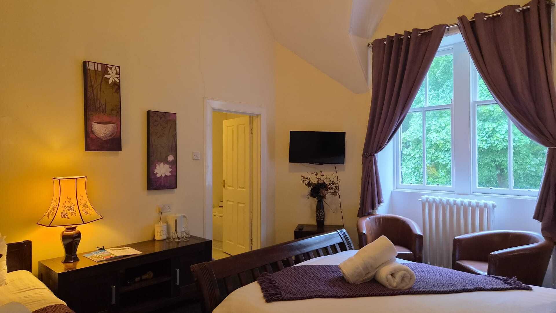 Quarto de hotel com cama, escrivaninha, cadeira, televisão e janela com cortinas.