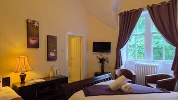 Quarto de hotel com cama, escrivaninha, cadeira, televisão e janela com cortinas.