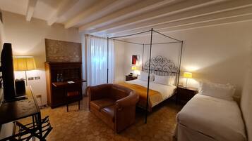 Quarto de hotel com cama de dossel, poltrona de couro, escrivaninha com luminária e minibar.