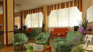 Uma sala de estar ampla com sofás estofados verdes, uma mesa de centro de vidro e uma janela grande com cortinas listradas.