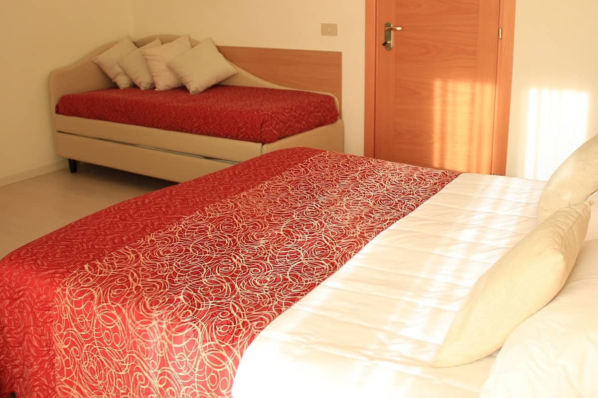 Quarto com cama, sofá-cama e porta de madeira.