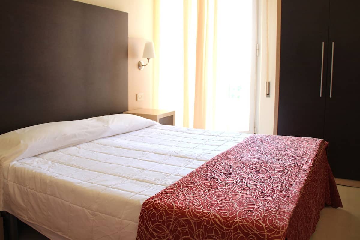 Quarto de hotel com uma cama, mesa de cabeceira, abajur e guarda-roupa.