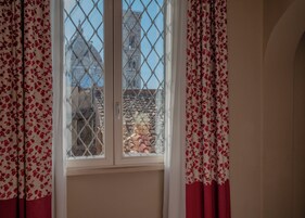 Janela com cortinas florais e vista para um edifício de arquitetura marcante.