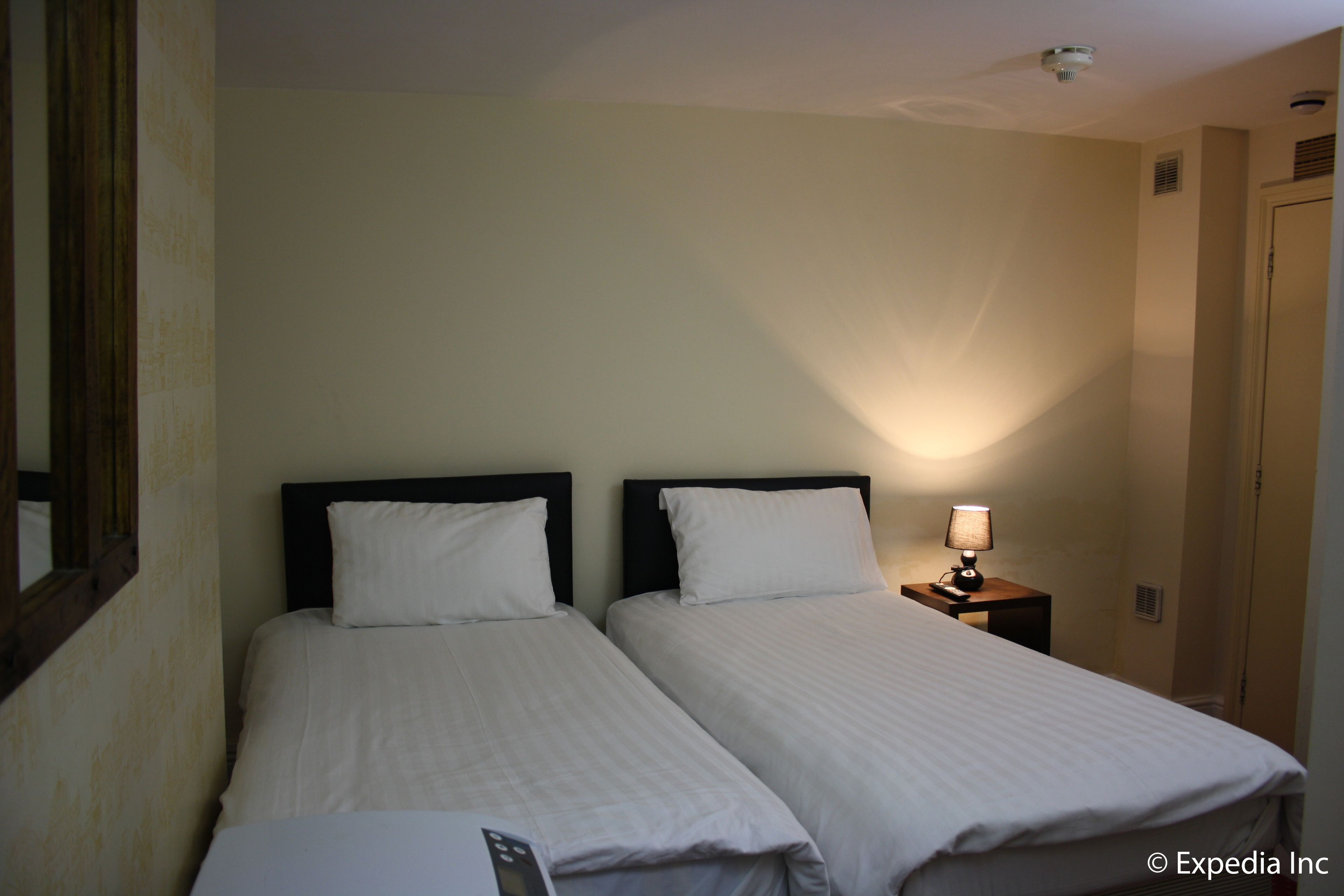 Quarto de hotel com duas camas de solteiro, mesa de cabeceira com abajur e uma porta.