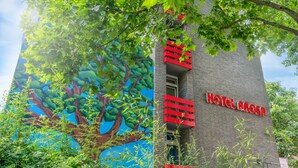 Fachada de hotel com um mural de uma árvore e o nome 'HOTEL ROSA' em letras vermelhas.