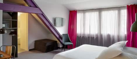 Quarto de hotel com cama, escrivaninha, cadeira, televisão e escada.