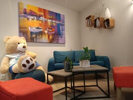 Uma sala de estar aconchegante com um urso de pelúcia grande, um sofá azul, uma mesa de centro e uma pintura abstrata colorida na parede.